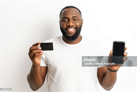 빈 화면으로 직불 카드와 스마트 폰을 들고 아프리카 계 미국인을 웃고 있습니다 Brand Name Mobile Payment에 대한 스톡 사진 및 기타 이미지 Brand