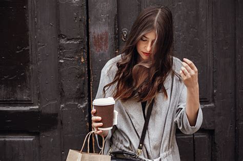 컵 커피와 가방 도시 거리에 오래 된 나무로 되는 문 서의 화려한 젊은 여자 아름 다운 바람 머리 시간을 즐기고 쇼핑 행복 Hipster 세련 된 소녀 가방에 대한 스톡