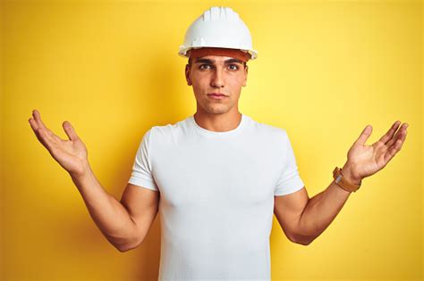 노란색 고립 된 배경 단서와 팔과 손을 들고 혼란 스러운 표정 위에 건설 헬멧을 착용 하는 젊은 잘 생긴 남자 의심 개념 감정에 대한 스톡 사진 및 기타 이미지 Istock