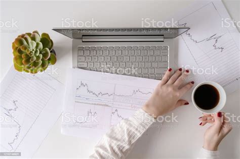 커피 한 잔과 함께 사무실 테이블에 앉아 종이에 인쇄 된 그래픽과 차트와 노트북에서 작업하는 동안 여성 프리랜서 작업 및 노트북의 키보드에 입력 플랫 레이 거래자에 대한
