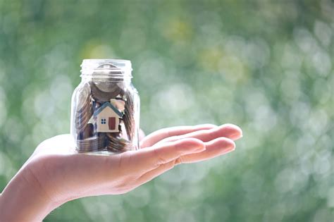 여성 손 의 부드러운 초점 은 자연 녹색 배경 비즈니스 투자 및 부동산 개념에 유리 병에 모델 하우스와 금화 돈을 들고 개념에