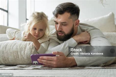 수염이 있는 쾌활한 아빠와 그의 어린 딸이 스마트폰으로 비디오를 보고 거실 바닥에 즐겁게 누워 웃고 있습니다 2명에 대한 스톡 사진 및 기타 이미지 Istock