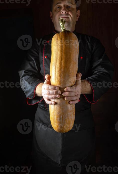 A Skilled Chef Stands In A Dimly Lit Kitchen Holding A Massive Squash