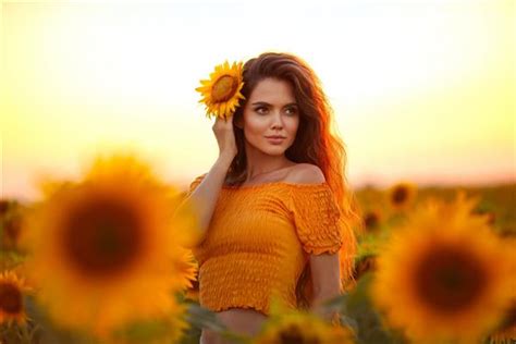 دختر جوان زیبا در حال لذت بردن از طبیعت در مزرعه آفتابگردان در غروب آفتاب تابستان زن سبزه جذاب