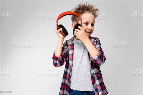 잘생긴 소년 격자 무늬 셔츠 회색 셔츠와 청바지에 회색 배경에 서 있다 빨간 헤드폰에서 소년입니다 소년은 그의 헤드폰에서 했다 감정에 대한 스톡 사진 및 기타 이미지