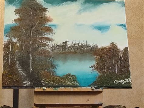 An Easel Sitting On Top Of A Wooden Table Next To A Painting With Trees In The Background