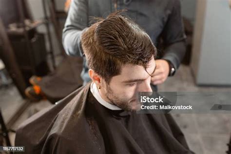마스터는 이발소에서 남자의 머리와 수염을 잘라 미용사는 젊은 남자를위한 헤어 스타일을만든다 이발소에서 클리퍼 기계와 이발사 작업 2명에 대한 스톡 사진 및 기타 이미지