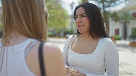 Two Women Engaging In A Friendly Conversation Outdoors In A Sunny Urban Park Setting Stock Video