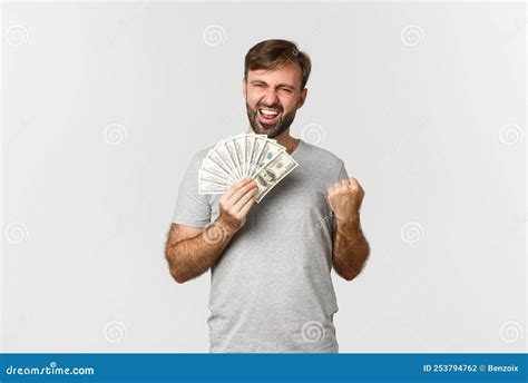 Pleased Smiling Man With Beard Wearing Gray T Shirt Rejoicing And Winning Cash Holding Money