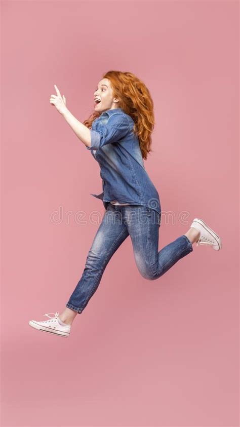 Redhead Girl Jumping And Pointing Finger Aside On Pink Background Stock