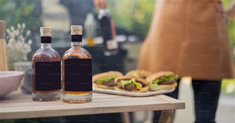 햄버거가 있는 테이블에 리큐어 또는 베리 팅크가 있는 병 배경에서 굽고 있는 사람들 복사 붙여넣기를 위한 빈 레이블이 있는 병에 클로즈업 사진 Unsplash의