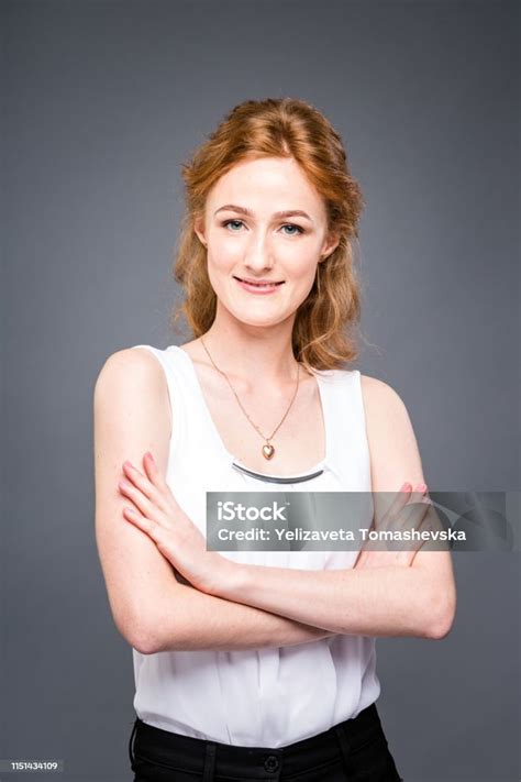 회색 고립 된 배경에 스튜디오에서 젊은 빨간 머리 아름다운 소녀의 초상화 한 여성이 팔을 접고 짧은 소매가 달린 흰색 셔츠를 입고 미소짓고 있다 비즈니스 개념 귀여운에 대한