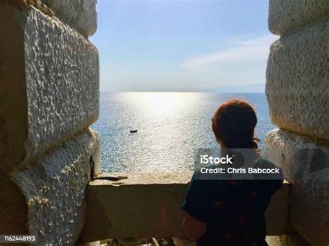 한 젊은 여성이 광활한 바다를 바라보고 있는 오래된 돌 종탑 꼭대기에 홀로 서 있었다 크로아티아 로비니의 종탑 꼭대기에 있는 이 곳은 눈부신 아드리아 해를 바라보고 있습니다