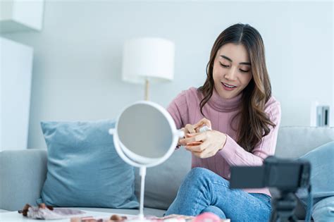 아시아 여성 동영상 블로거가 카메라와 대화를 나누며 집에서 화장품을 검토합니다 아름다운 뷰티 블로거 인플루언서 소녀는 소파와