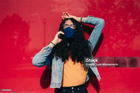 곱슬 머리와 얼굴 마스크를 가진 Lgtb 트랜스 젠더 소녀는 빨간 벽에 그녀의 휴대 전화로 전화 코로나바이러스 개념 20 24세에 대한 스톡 사진 및 기타 이미지 Istock