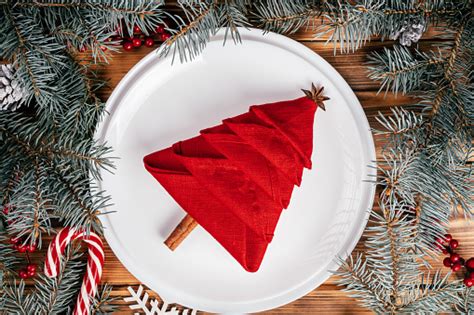 린넨 냅킨은 가문비나무 가지 사이에 흰색 접시에 크리스마스 트리 모양으로 접혀 새해 테이블 설정 위쪽 보기 냅킨에 대한 스톡 사진 및 기타 이미지 Istock