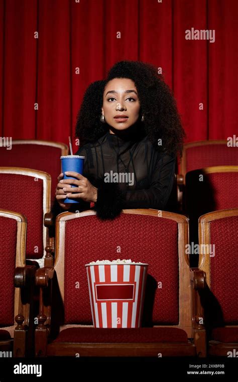 A Stylish Woman Sits In A Movie Theater Seat Holding A Drink And