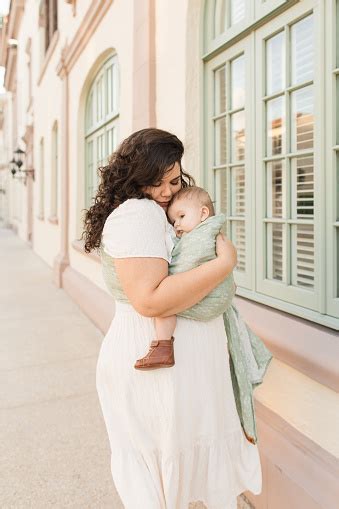 30 세의 쿠바 어머니와 5 개월 된 쿠바 계 미국인 아들과 현자 녹색 반지 슬링 베이비 캐리어를 타고 2022 년 봄에 플로리다 팜 비치 의 우아한 보도를 따라 걷고