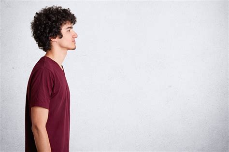 프로필 샷 어두운 곱슬 머리와 잘생긴 젊은 남자 캐주얼 마 룬 T 셔츠를 입고 복사 공간을 보면 광고 또는 홍보 텍스트에 대 한 여유 공간 흰 벽에 대 한 의미 남자에 대한