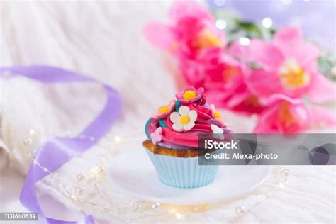 분홍색 튤립 Bokeh 조명과 새틴 리본이 흐린 배경에 화려한 꽃으로 장식 된 크림 색 색상의 상단 근접 촬영 컵 케이크 3월에