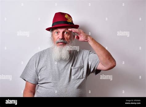 An Old American Male With A Grey Shirt And Red Fedora Hat Saluting