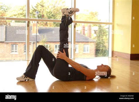 Female Doing Lying Hamstring Stretch On Wooden Gym Floor With Large Natural Light Window Stock