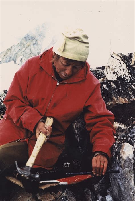 A Woman In A Red Jacket And White Toque Sits Leaned Up Against The Rock