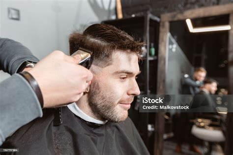 마스터는 이발소에서 남자의 머리와 수염을 잘라 미용사는 젊은 남자를위한 헤어 스타일을만든다 이발소에서 클리퍼 기계와 이발사 작업