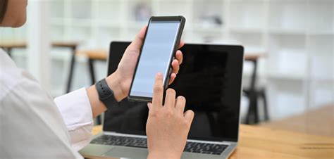 자른 이미지 여성은 컴퓨터 노트북 앞에 앉아있는 동안 흰색 빈 화면 스마트 폰을 들고있다 공란에 대한 스톡 사진 및 기타 이미지