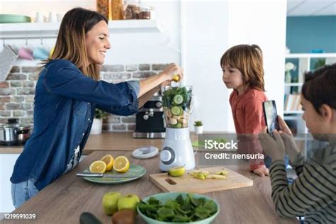 동생이 휴대 전화로 사진을 찍는 동안 어머니가 믹서기로 해독 주스를 준비하도록 돕는 소년 스무디에 대한 스톡 사진 및 기타 이미지 스무디 만들기 녹색 Istock