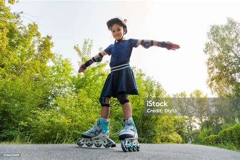 한 어린이가 공원의 녹색 식물 의 배경에 팔을 뻗어 롤러 스케이트를 타고 있습니다 공원에서 롤러 스케이트에 어린 소녀 균형 균형 균형 행위 건강한 생활방식에 대한 스톡 사진