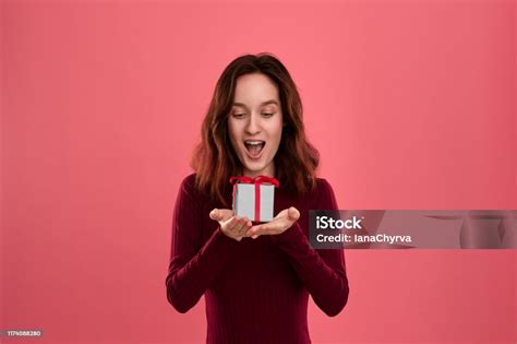 두 손이 어두운 분홍색 배경에 고립되어 서서 카메라에 미소와 리본현재 상자를 들고 흥분 예쁜 갈색 머리 소녀 특별 행사를