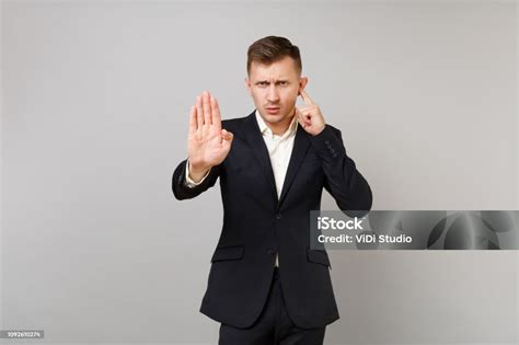우려 젊은 비즈니스 남자가 고전적인 검은 양복 손가락으로 귀를 덮고 손바닥 회색 배경에 고립 중지 제스처를 보여주는 있다 성과 경력 부 비즈니스 개념입니다 복사 공간을