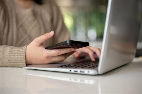 Premium Photo A Woman Holding A Smartphone While Typing On Her Laptop Keyboard Working On Her