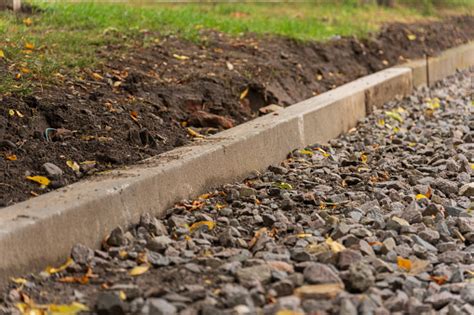 새로 설치된 콘크리트 연석은 자갈 길을 따라 늘어서 있으며 흙빛 색조가 주변 녹지와 조화를 이룹니다 낙엽은 고요한 분위기에 가을 분위기를 더합니다 0명에 대한 스톡 사진 및
