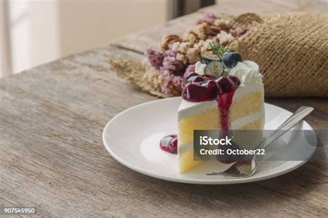 나무 테이블 창 근처에 흰색 접시에 블루베리 크림 케이크 바닐라 스펀지 케이크 장식 낙농 휘 핑된 크림과 블루베리 소스 너무 부드럽고 달 콤 하 고 맛 있는 수 제 베이커리