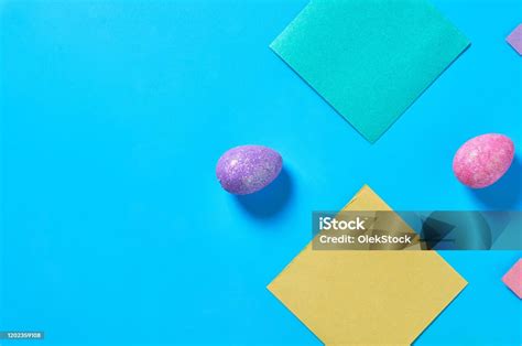 빈 사각형 종이 스티커 근처 반짝이 많은 다채로운 계란 부엌에 파란색 책상에 놓여있다 부활절 개념입니다 텍스트의 공백입니다 맨