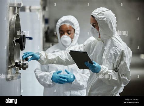 Side View Of Female Process Technician In Hazmat Suit Using Tablet Computer Inspecting Stainless