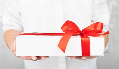 빨간 활이 달린 흰색 선물 상자를 들고있는 여성 손의 클로즈업 여자는 빨간 리본이 달린 흰색 상자를 들고 있습니다 기념일에 대한