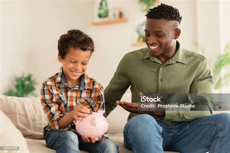 실내에서 돼지 저금통에 동전을 넣는 행복한 아들과 아프리카 아빠 25 29세에 대한 스톡 사진 및 기타 이미지 25 29세 8 9 살 가정 생활 Istock
