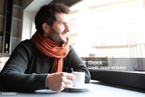 카페테리아에서 커피를 마시며 이른 아침을 즐기며 창문 밖을 내다보는 연금적이고 행복한 청년 공간을 복사합니다 남자에 대한 스톡