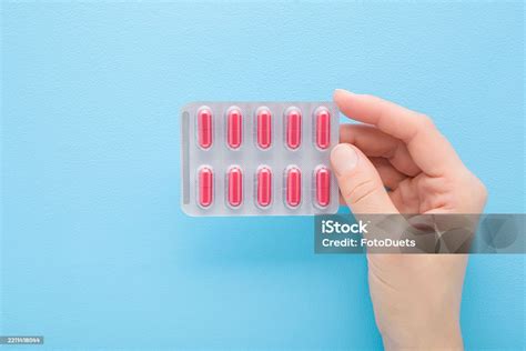 젊은 성인 여자 손 손가락을 들고 밝은 파란색 테이블 배경에 혈액의 철 수준을 향상시키기 위해 빨간 알약과 함께 물집 팩을 보여줍니다 파스텔 색상 근접 촬영 하향식 보기