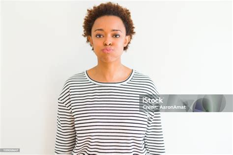 젊은 아름 다운 아프리카계 미국인 여자 재미 있는 얼굴 흰색 배경 퍼 핑 뺨에 줄무늬 스웨터를 입고 입에 공기 미친 표정으로