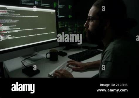 Bearded Programmer Writing Code Sitting At Desk With Multiple Monitor