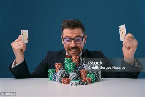 안경을 쓴 동료 칩 더미가 있는 테이블에 앉아 두 장의 카드 놀이를 들고 파란 배경에서 포즈를 취하고 있는 검은 색 정장 포커 카지노 클로즈업 2명에 대한 스톡 사진 및
