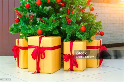 실내에 설치된 빨간 공과 반짝이는 조명으로 장식 된 크리스마스 트리 크리스마스와 새해를 위한 빨간 새틴 실크 리본이 달린 판지 종이 상자 선물 0명에 대한 스톡 사진 및