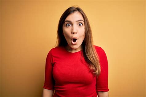 노란색 고립 된 배경에 캐주얼 빨간 티셔츠를 입고 아름다운 젊은 여성은 두려워하고 깜짝 표정 두려움과 흥분 얼굴로 충격 T