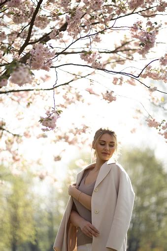아름 다운 금발 젊은 여 자가 봄 벚꽃 공원에서 자연과 자유 시간을 즐기는 그녀의 여행 관광 자유 시간을 입고 흰색 바지와 T 셔츠 베이 지 색 재킷 건물 외관에 대한 스톡