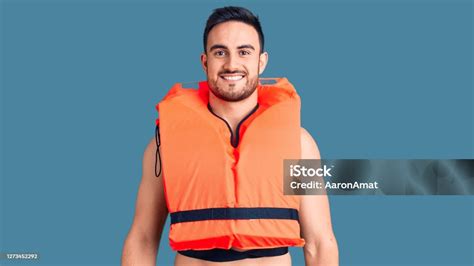구명조끼를 입은 젊은 잘생긴 남자는 긍정적이고 행복한 서 있고 치아를 보여주는 자신감있는 미소로 미소를 지었습니다 구명 조끼에 대한 스톡 사진 및 기타 이미지 Istock