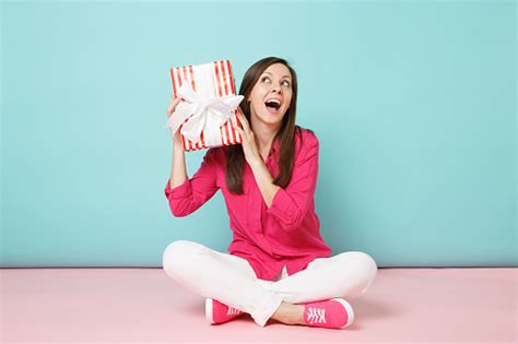 바닥에 앉아 장미 셔츠 블라우스 흰색 바지에 전체 길이의 초상화 여자 밝은 분홍색 파란색 파스텔 벽 배경 스튜디오에 고립 된 선물 상자를 개최 합니다 패션 라이프 스타일